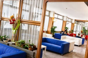 Um hall de hotel com sofás azuis, uma área de recepção e plantas em vasos.