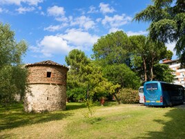 Uma construção de pedra, um ônibus estacionado e árvores numa área gramada.