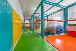 Espaço de recreação infantil com piso verde, redes de proteção e paredes coloridas.