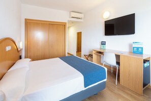 Quarto de hotel com cama, escrivaninha, cadeira e televisão de tela plana na parede.