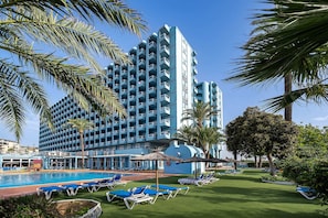 Um hotel com piscina, espreguiçadeiras e palmeiras.