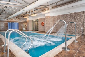 Piscina interna com um recurso de água transparente, rodeada por paredes revestidas de azulejos e grades de metal.