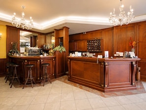 Uma área de bar com painéis de madeira, uma máquina de café e banquetas.