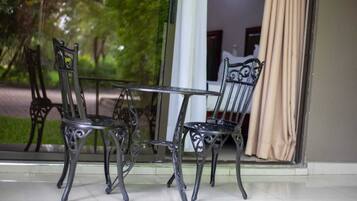 Quarto com porta de vidro que dá para um jardim, uma mesa com cadeiras e vista para árvores lá fora.