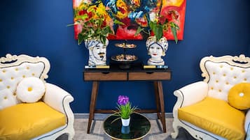 Um quarto com dois sofás brancos com almofadas amarelas, uma mesinha com objetos decorativos e um quadro colorido na parede.