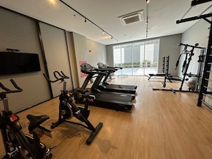 Uma academia com equipamentos de ginástica, televisão e janelas amplas.
