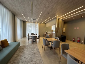 Quarto de hotel moderno com área de refeições, sofá, tapete e extintor de incêndio.