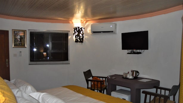 Quarto de hotel com uma cama, uma escrivaninha com cadeira, televisão e ar condicionado.