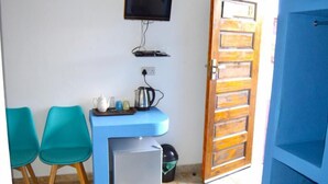 Quarto com uma pequena cozinha compacta, televisão fixada na parede e uma porta com número.
