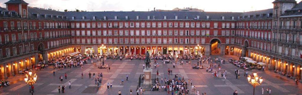 Pátio histórico com uma estátua central, rodeado por edifícios com vários andares e varandas.