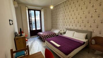 Quarto com cama, escrivaninha, cadeira, mesinha e janela com persianas.