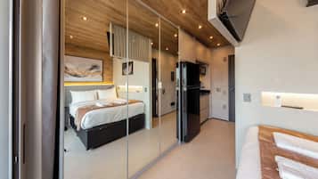 Quarto moderno com cama grande, armário embutido e cozinha equipada com frigorífico e micro-ondas.