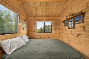 Um quarto de cabana de madeira com uma cama, uma janela e uma prateleira com quadros.