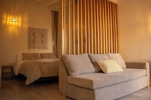 Quarto com cama, sofá, divisória de ripas de madeira e luminária fixada na parede.