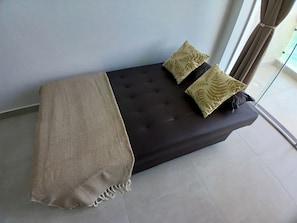 Cama com cabeceira escura, duas almofadas estampadas e um cobertor bege.