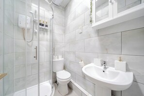 Uma casa de banho moderna com chuveiro em cabine de vidro, sanita branca, lavatório com espelho e artigos de higiene pessoal na parede.
