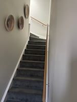 Uma escadaria com carpete, corrimão de madeira e parede branca.