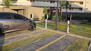 Uma área de estacionamento com estações de carregamento para veículos elétricos, um carro e um edifício com design moderno ao fundo.