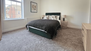 Quarto com cama, mesas de cabeceira, janela, radiador e um quadro na parede.