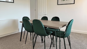 Uma área de refeições com uma mesa retangular, seis cadeiras e duas obras de arte emolduradas nas paredes.