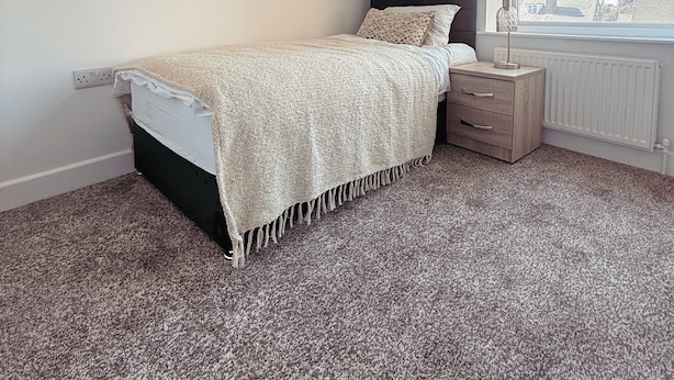 Quarto com cama, mesa de cabeceira, janela e radiador.