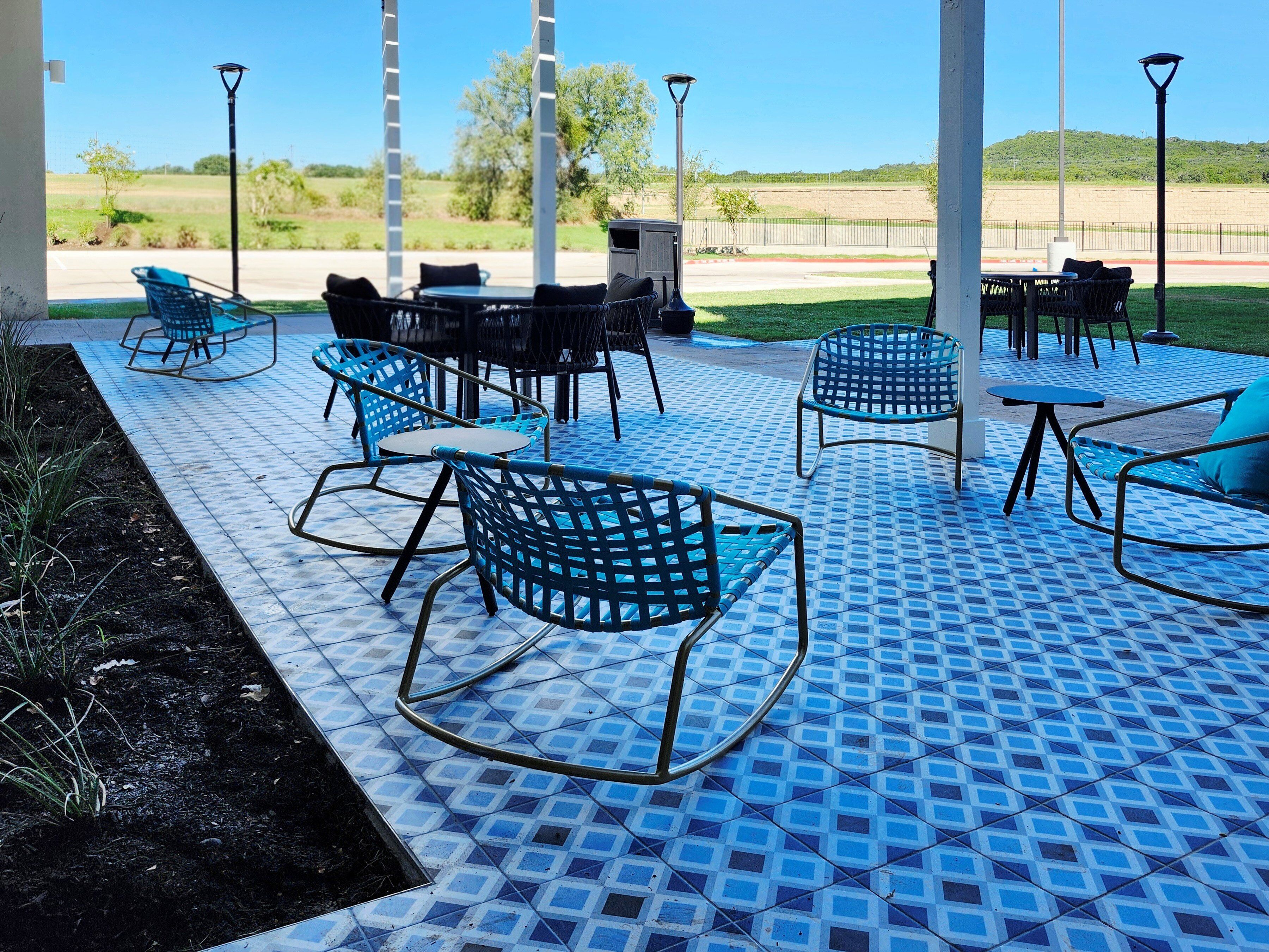 Um pátio externo com piso azul estampado, cadeiras e mesas de metal.