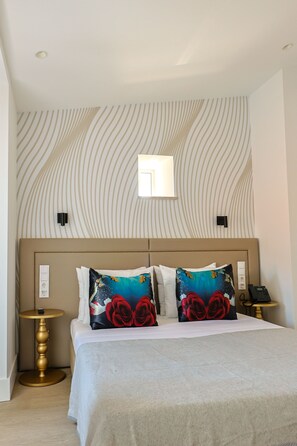 Quarto de hotel com cama, mesa de cabeceira, luminária na parede e telefone.