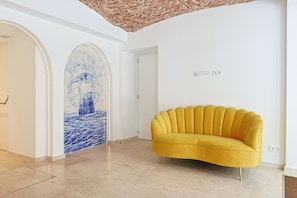 Quarto com sofá amarelo, piso de azulejos e parede com um mural de navio.