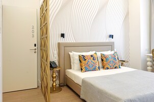 Quarto de hotel com cama, mesa de cabeceira, telefone e painel decorativo na parede.