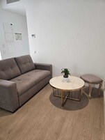 Uma sala de estar moderna com um sofá cinzento, uma mesa de centro redonda com uma planta e um pequeno banquinho.