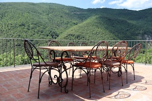 Um terraço com mesa e cadeiras, com vista para uma encosta arborizada.