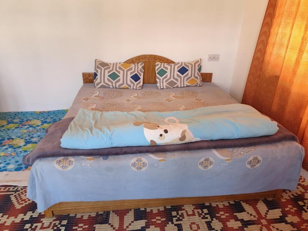 Uma cama com roupa de cama e almofadas estampadas, um tapete padronizado e uma parede com uma tomada.