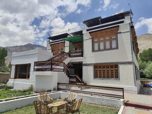 Um edifício de dois andares com varanda, escadaria e uma pequena área externa com cadeiras.