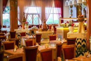 Restaurante com mesas e cadeiras redondas, uma fonte decorativa central e vista para o verde lá fora.