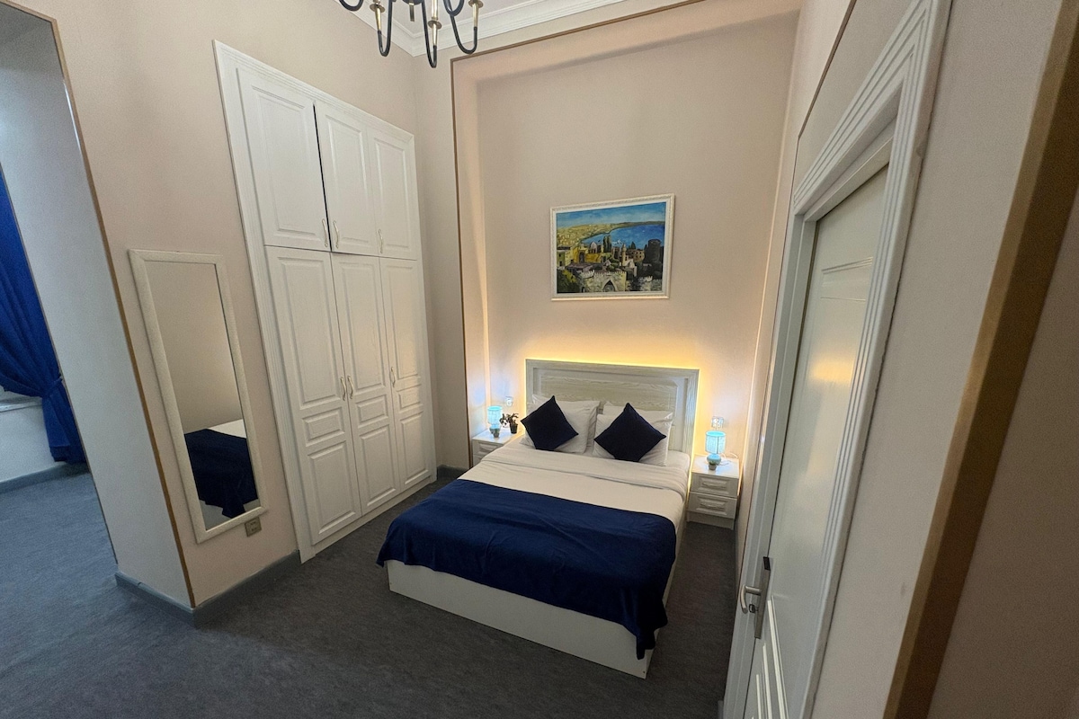 Quarto com cama, mesa de cabeceira, espelho, guarda-roupa e um quadro na parede.