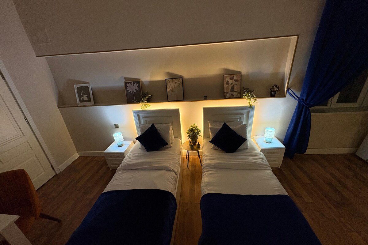 Cama de casal com cabeceira, mesas de cabeceira e criado-mudo com abajur.