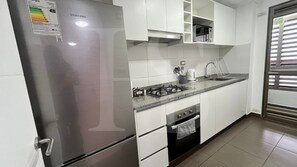 Uma cozinha com geladeira de aço inoxidável, fogão a gás, micro-ondas e armários brancos.
