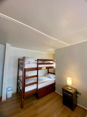 Uma cama beliche com mesa de cabeceira e luminária, soalho de madeira e teto branco.