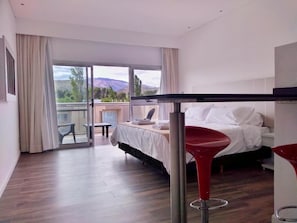 Quarto de hotel moderno com uma cama, um banquinho vermelho e vista para o exterior.