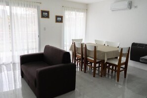 Um quarto com sofá, mesa de jantar com cadeiras e ar condicionado.