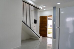 Um corredor com escadas, uma porta e uma geladeira.