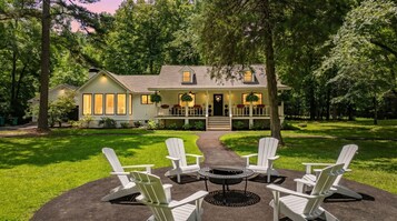 Uma casa com varanda, lareira e quatro cadeiras Adirondack.