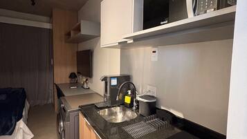 Uma cozinha compacta com micro-ondas integrado, cafeteira e pia.