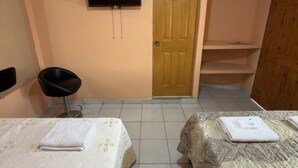 Quarto com duas camas, televisão, porta e uma cadeira.