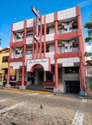 Um hotel com fachada marcante em vermelho e branco, um letreiro bem visível e uma entrada ampla.