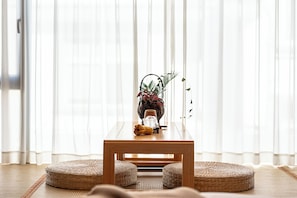 Um quarto com uma mesa de madeira, pufes trançados e um arranjo de plantas.