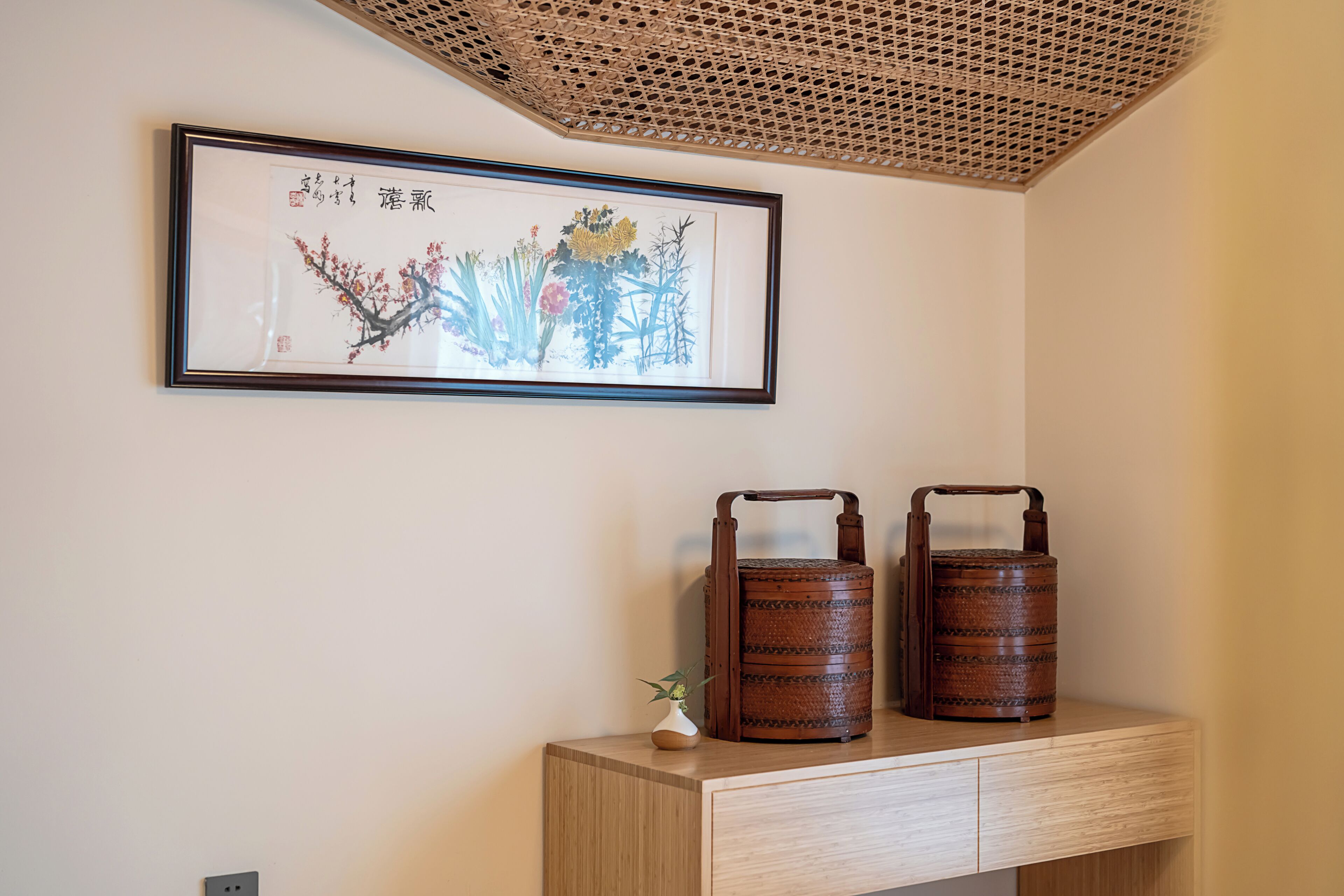 Uma moldura com uma obra de arte na parede, um armário de madeira com dois recipientes e um teto com design em treliça.