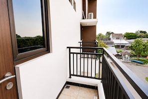Uma varanda residencial com grade de metal preta, uma janela e vista para um rio e edifícios.