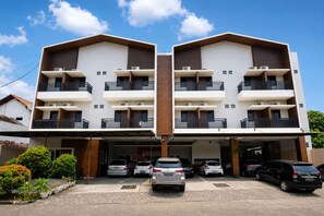 Um edifício residencial de vários andares com varandas, uma área de estacionamento coberta e uma fila de vasos de plantas em primeiro plano.