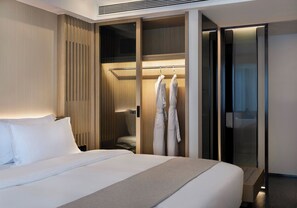Quarto de hotel com uma cama grande, um guarda-roupa com espelho e um porta-robes com duas toucas de banho.